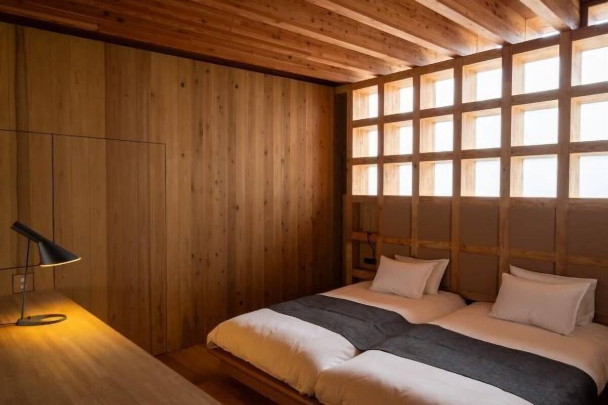 Quarto de madeira com cama, escrivaninha e abajur.