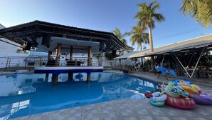 Piscina com área coberta, palmeiras e brinquedos infláveis.