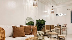 Sala de estar moderna com sofá branco, almofadas marrons, mesa de centro redonda de vime e uma grande planta em vaso.