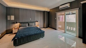 Quarto moderno com cama grande, mesa de cabeceira, ar condicionado fixado na parede e porta de vidro deslizante para uma varanda.