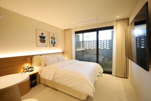 Quarto de hotel moderno com uma cama grande, mesa de cabeceira, televisão integrada e vista para o exterior através de uma porta de correr de vidro.