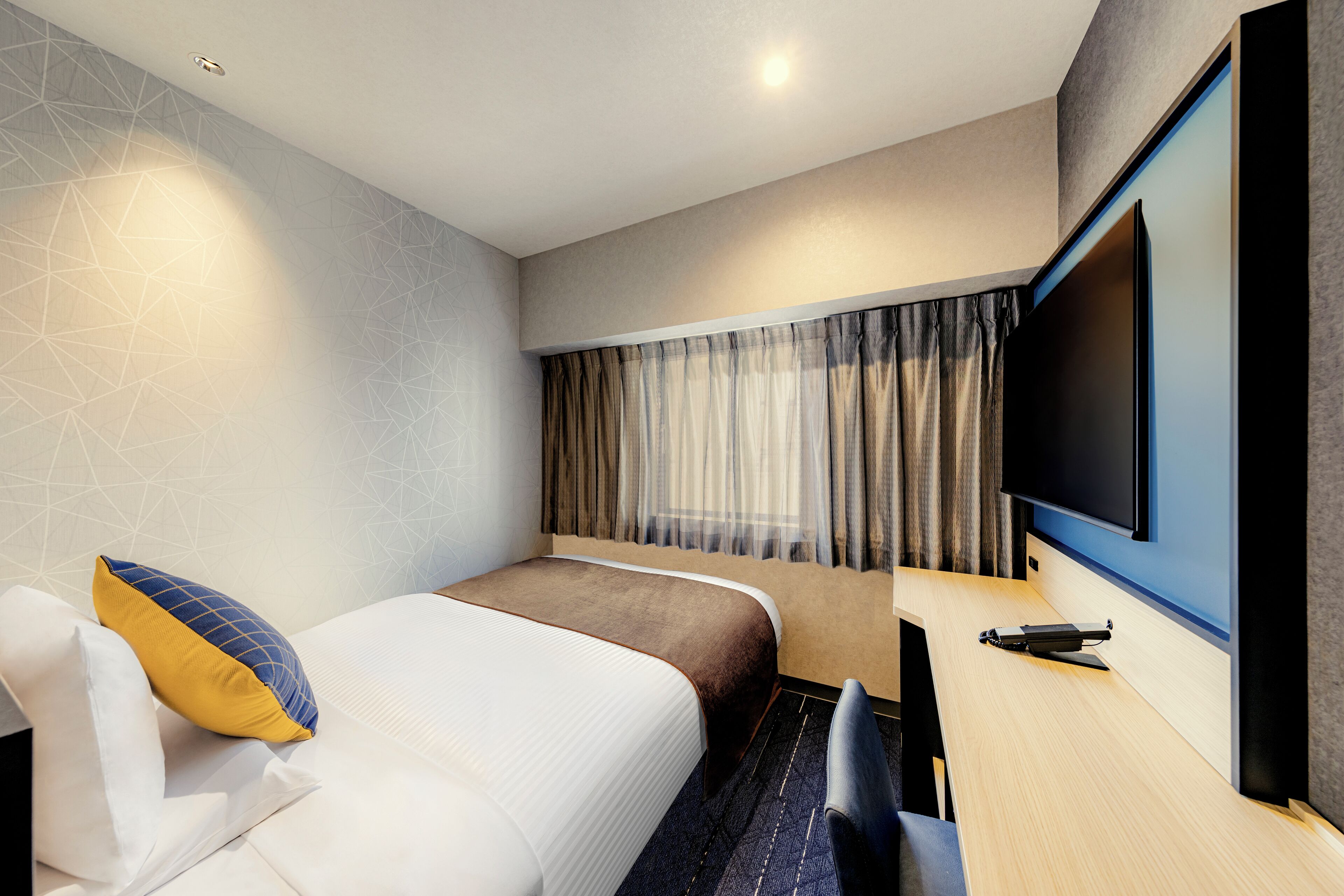 Quarto de hotel com cama, escrivaninha, televisão de tela plana e janela com cortinas.