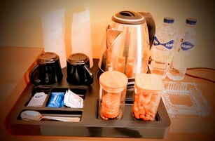 Uma estação de café com cafeteira, dois termos, um pote de lanches e água engarrafada.