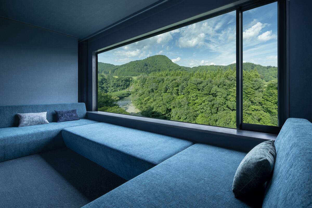 Quarto moderno com uma janela grande que oferece vista para uma encosta arborizada.