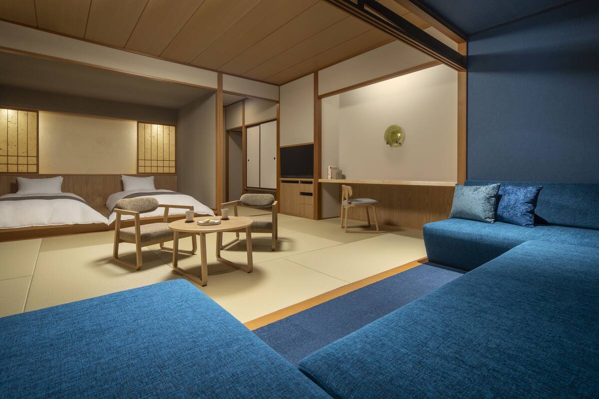 Um quarto em estilo japonês tradicional, com tatames, teto de madeira baixo e um sofá azul.