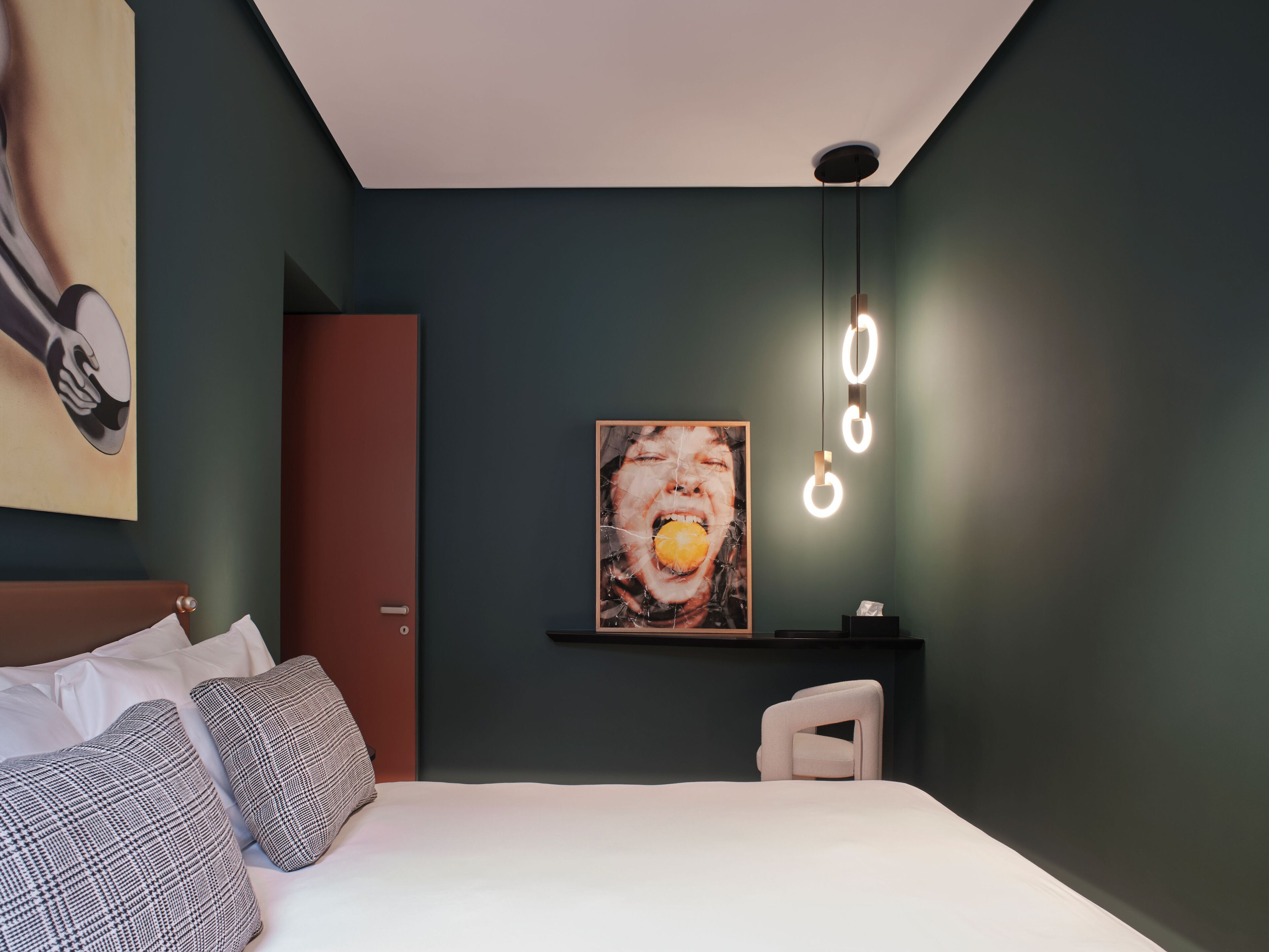 Um quarto moderno com cama, almofadas, um quadro, uma cadeira e uma estante com luminária.