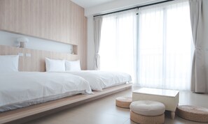 Quarto de hotel moderno com uma cama grande, mesas de cabeceira e vista da cidade através de amplas janelas.