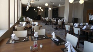 Restaurante com várias mesas preparadas para refeições, apresentando um interior moderno com iluminação pendente e vista para o exterior.