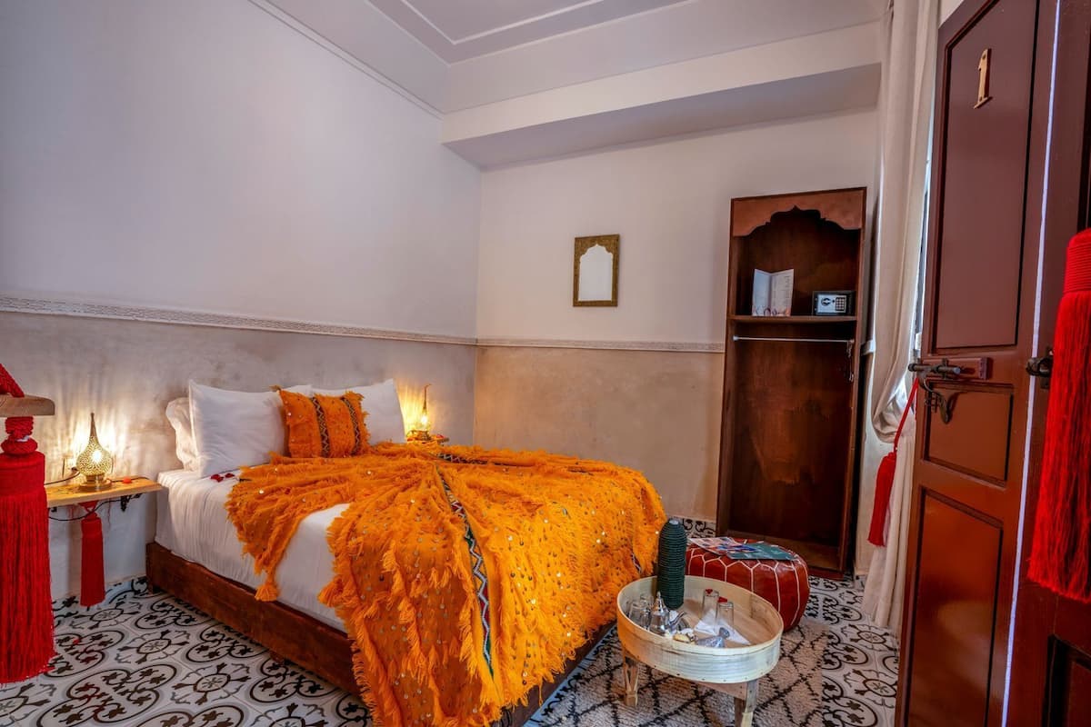 Um quarto com uma cama, mesa de cabeceira, abajur, guarda-roupa e uma pequena mesa com um tabuleiro.