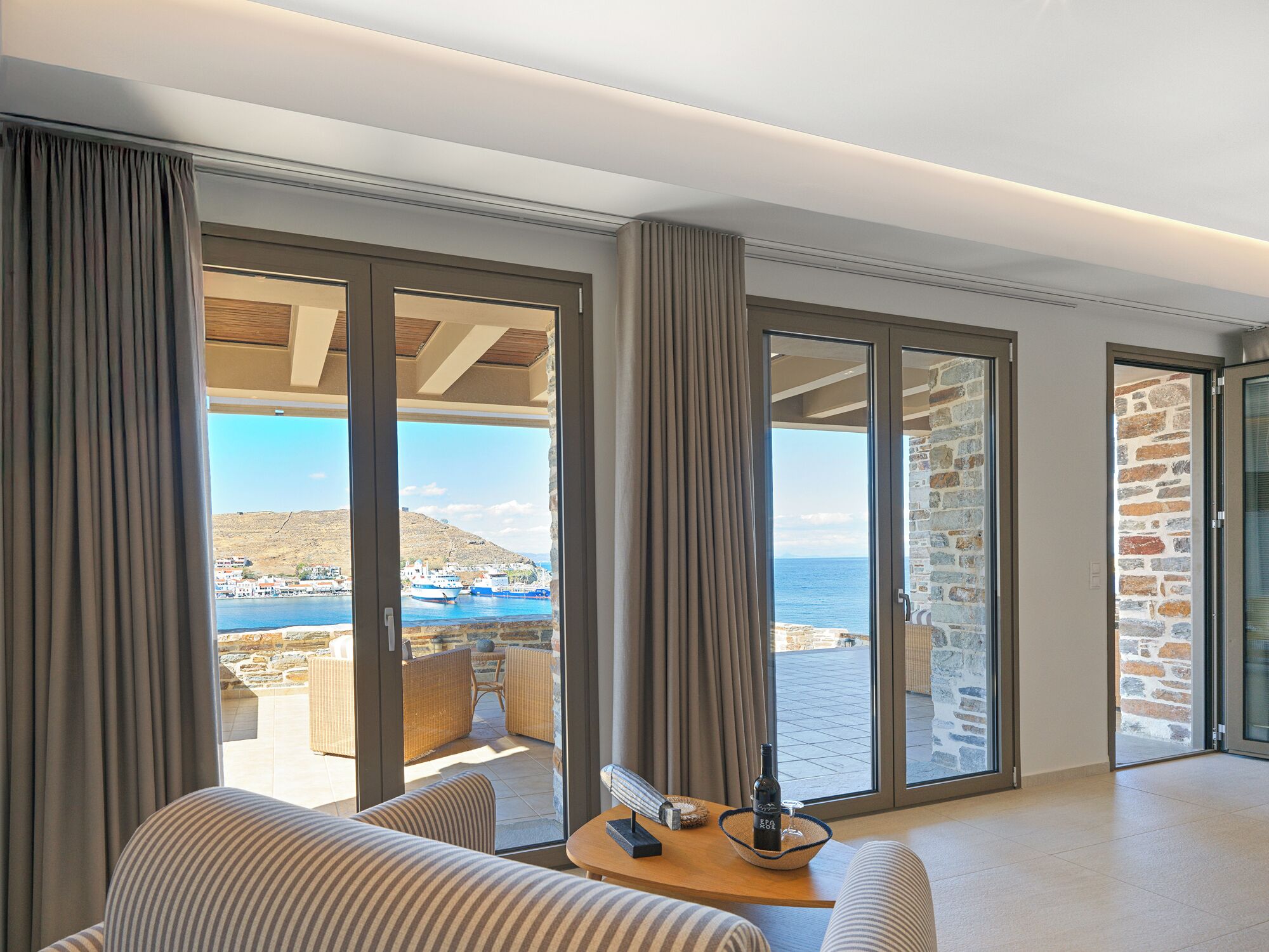 Quarto de hotel moderno com uma grande porta de vidro deslizante para uma varanda com vista para o mar e uma encosta.