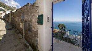 Um edifício costeiro com vista para o mar, um portão azul e uma escadaria que leva a um balcão.
