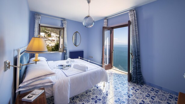 Quarto com uma cama, abajur, janela com vista e espelho na parede.