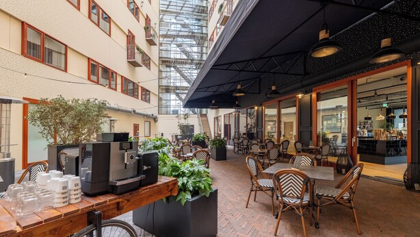 Um café no terraço com mesas ao ar livre, uma máquina de café e plantas em vasos.