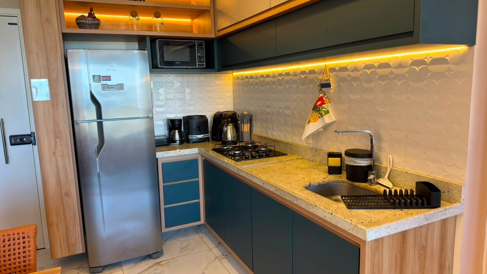 Cozinha compacta com geladeira, micro-ondas, cafeteira e pia.