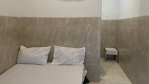Quarto com cama, duas almofadas, mesa de cabeceira e luminária fixada na parede.