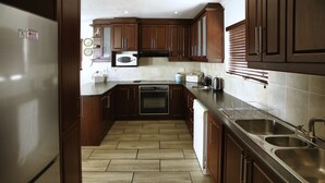 Cozinha com armários de madeira, geladeira de aço inoxidável, micro-ondas, forno e pia dupla.