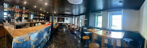 Uma área de bar com balcão de mármore, prateleiras cheias de garrafas e espaço para acomodar os hóspedes.