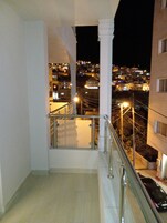 Vista noturna de uma varanda com guarda-corpo de metal, com vista para um horizonte urbano iluminado.