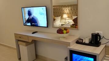 Quarto de hotel com escrivaninha, televisão, espelho e uma pequena tela.