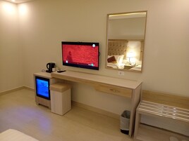 Quarto de hotel com televisão de tela plana, cafeteira, pequena mesa com gaveta, lixeira e cama com cabeceira.