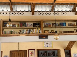 Um quarto com estantes de madeira repletas de livros e objetos decorativos, uma lâmpada pendurada e um quadro na parede.