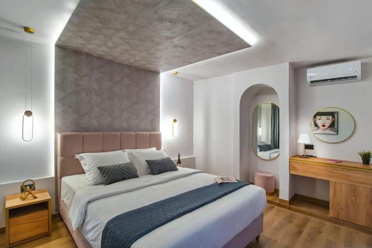 Quarto moderno com uma cama grande, mesas de cabeceira, uma cômoda com espelho e aparelho de ar condicionado.
