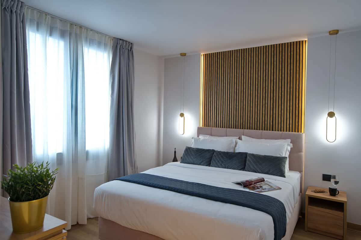 Quarto de hotel moderno com uma cama grande, uma mesa de cabeceira com abajur e um vaso de plantas.