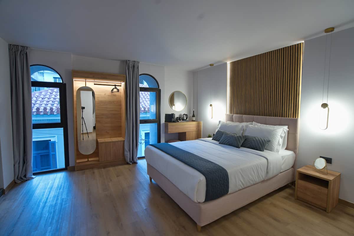 Quarto moderno com cama grande, mesas de cabeceira, espelho e vista através de uma janela em arco.
