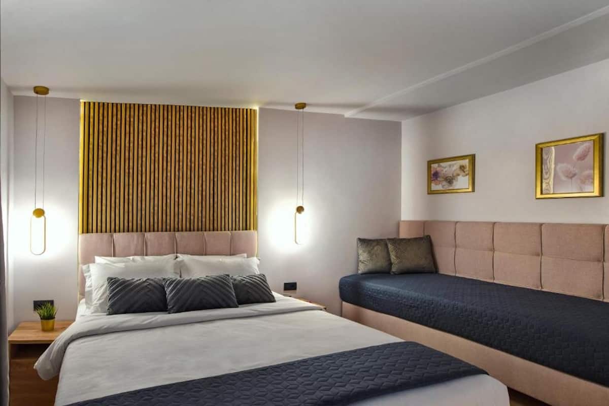 Quarto de hotel moderno com uma cama grande, um sofá menor e um painel decorativo na parede.