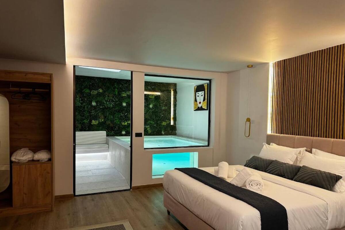 Quarto moderno com uma cama grande, porta de correr de vidro que dá para uma varanda e vista de um jardim exuberante.