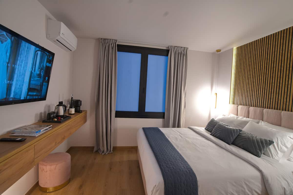 Quarto de hotel moderno com cama, escrivaninha com computador, janela com cortinas e ar condicionado fixado na parede.