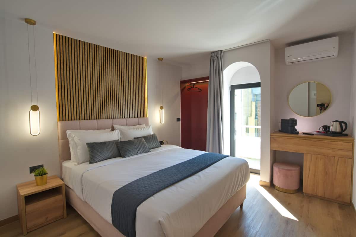 Um quarto moderno com uma cama grande, mesas de cabeceira, uma cabeceira de madeira, uma escrivaninha com um espelho e um aparelho de ar condicionado.