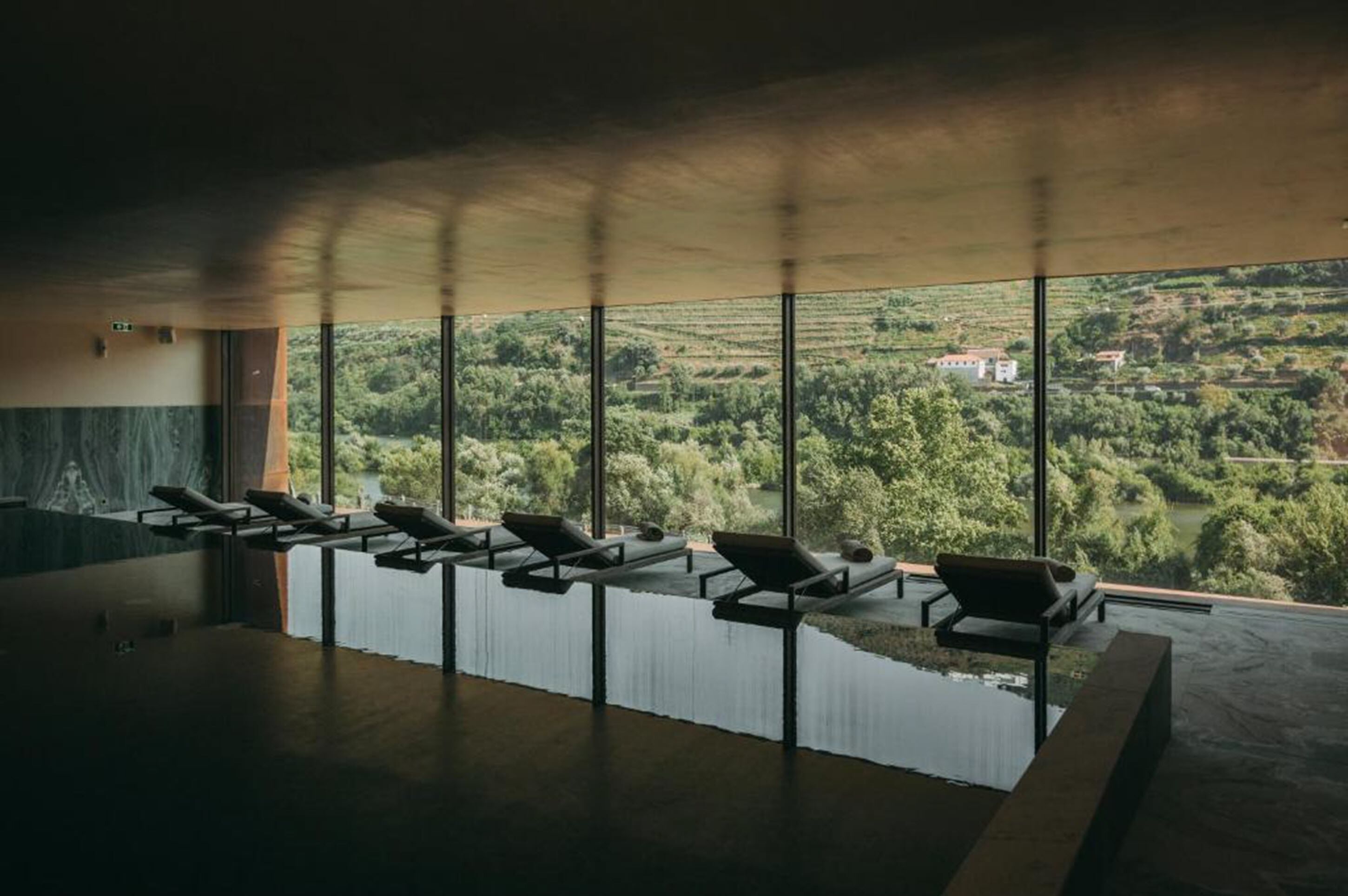 Piscina interior moderna com espreguiçadeiras e vista para uma paisagem exuberante.