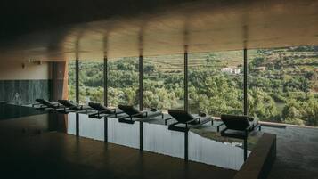 Piscina interior moderna com espreguiçadeiras e vista para uma paisagem exuberante.
