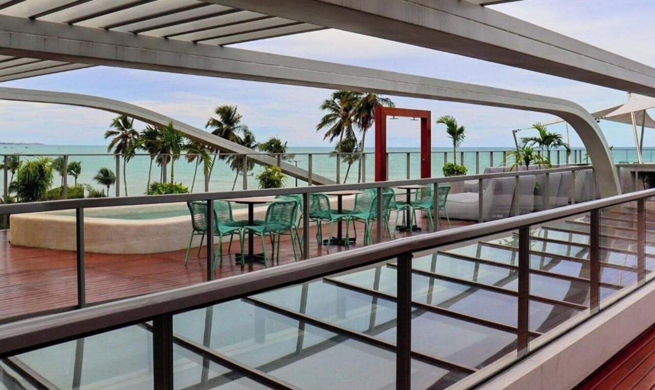 Um terraço com guarda-corpo de vidro, área de estar ao ar livre e vista para o oceano.