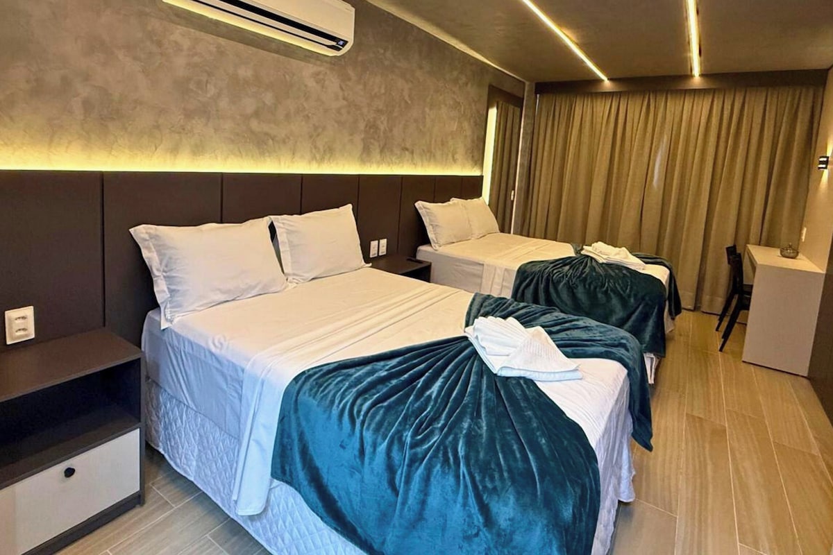 Quarto de hotel com duas camas, uma mesa de trabalho e uma televisão.