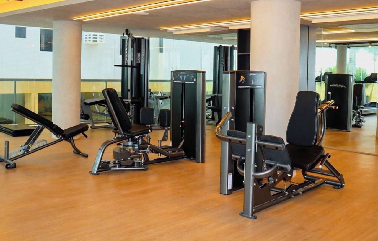 Uma academia com diversos equipamentos de exercícios, janelas amplas e piso de madeira.