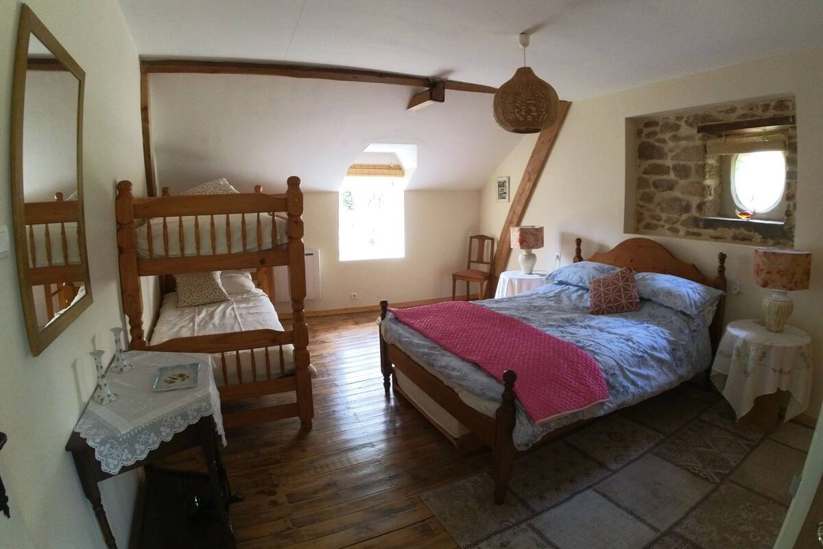 Quarto com cama beliche, uma cama de solteiro, uma mesinha e uma cadeira.