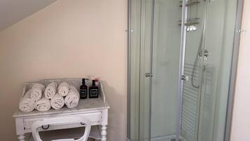 Um chuveiro com porta de vidro, uma mesa com toalhas enroladas e duas garrafas de shampoo.