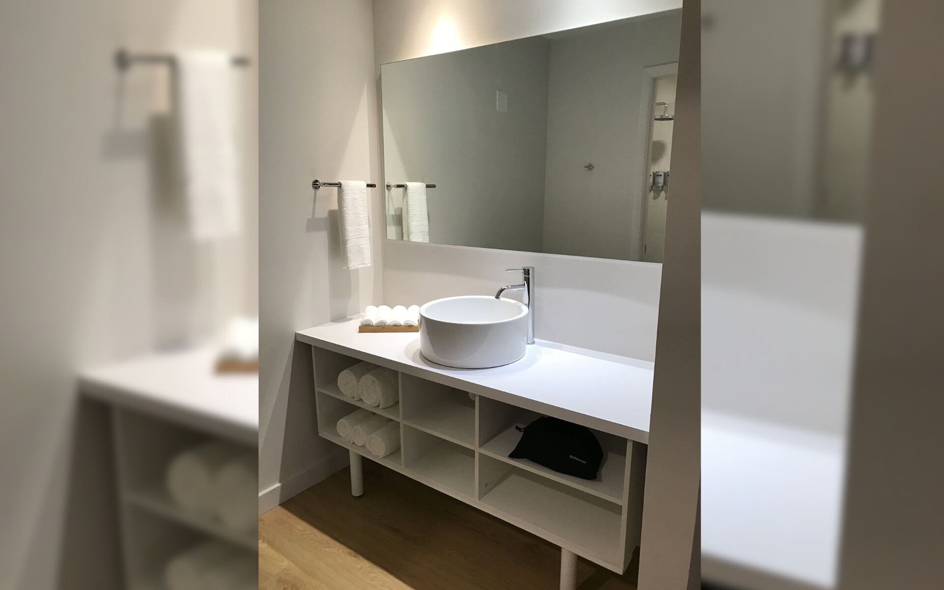 Casa de banho moderna com lavatório branco, espelho e prateleiras para toalhas.