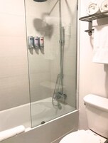 Divisória de chuveiro com paredes de vidro, vaso sanitário e porta-toalhas com toalhas.