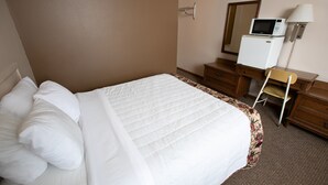 Quarto de hotel com cama, escrivaninha, cadeira, micro-ondas e luminária.