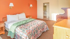 Quarto de hotel com cama, duas luminárias de cabeceira, mesa de cabeceira de madeira, penteadeira e porta para um banheiro.