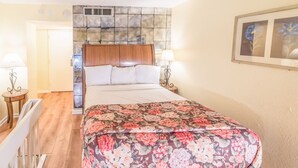 Quarto com cama de madeira, colcha floral, duas luminárias de mesa, parede de pedra e um quadro na parede.