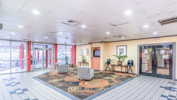 Um hall de hotel com piso xadrez, carpete estampado e um espaço de estar com cadeiras e uma mesa.