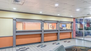 Uma área de recepção com balcão de check-in, espaço para sentar e porta de vidro que dá para o exterior.