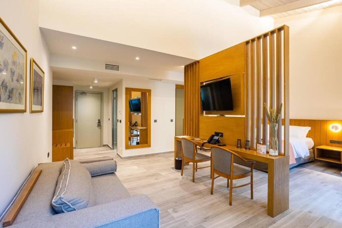 Quarto de hotel moderno com sofá, escrivaninha com cadeiras, televisão e cama.