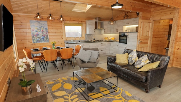 Interior acolhedor de uma cabana com área de jantar, sala de estar com sofá e mesa de centro, e cozinha com armários de madeira e fogão moderno.
