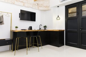 Cozinha moderna com bancada preta, banquetas douradas, pia preta e televisão fixada na parede.