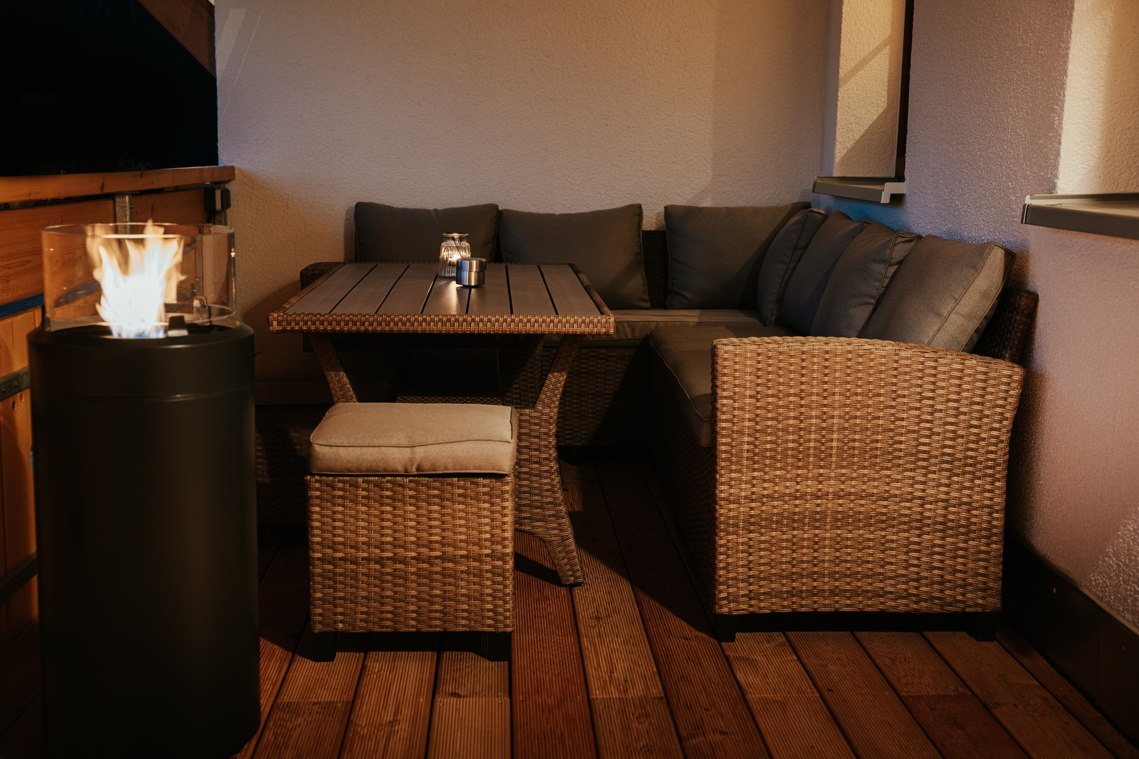 Uma área de estar ao ar livre aconchegante, com móveis de vime, uma mesa e uma lareira iluminada.